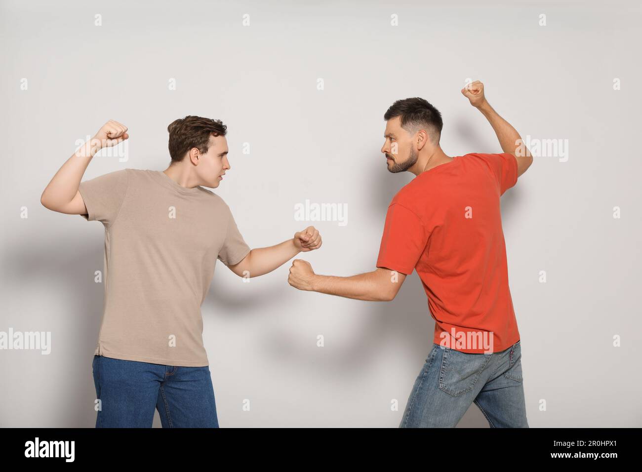 Two emotional men fighting on beige background Stock Photo - Alamy