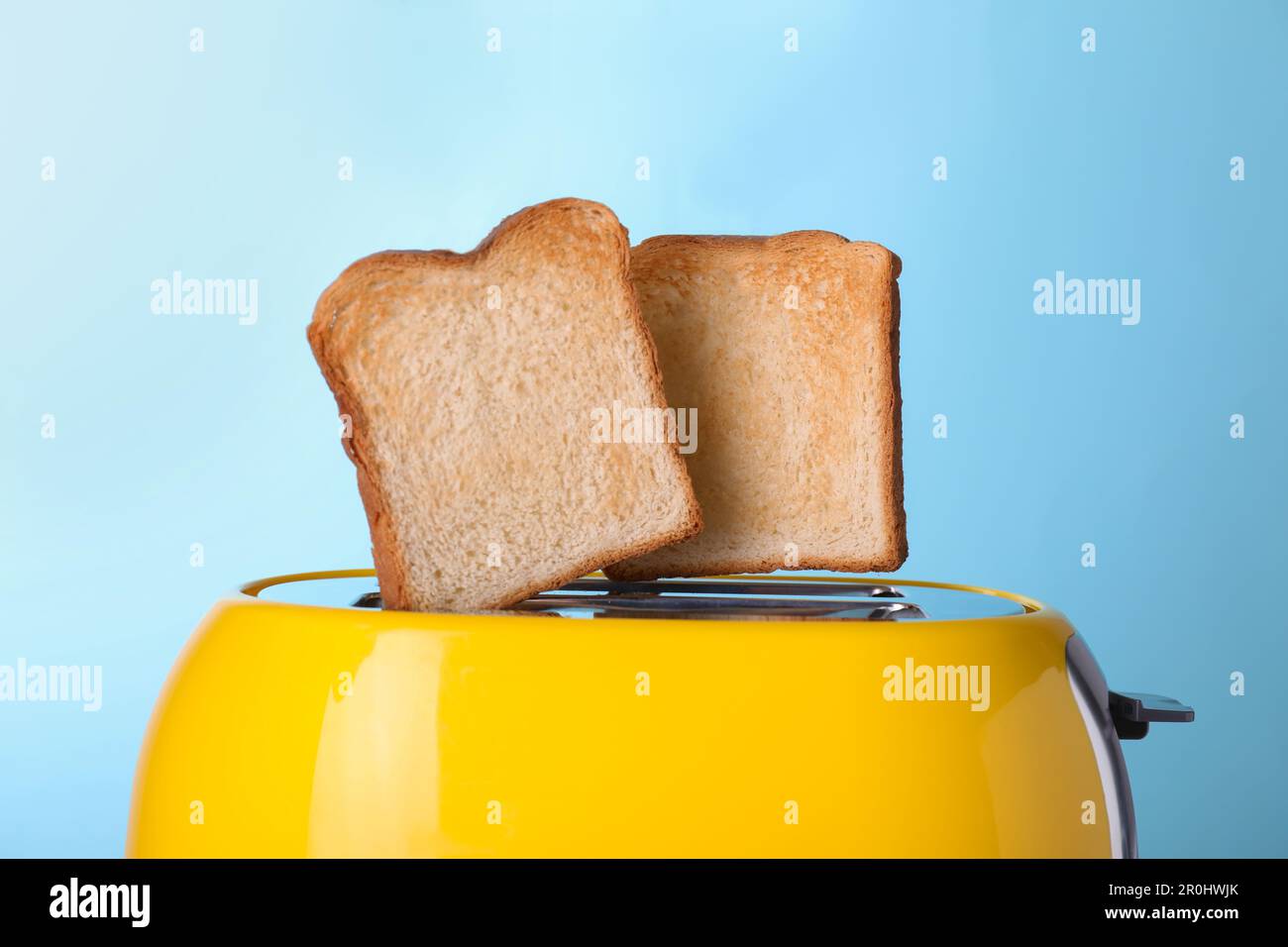 Yellow toaster with roasted bread against light blue background ...