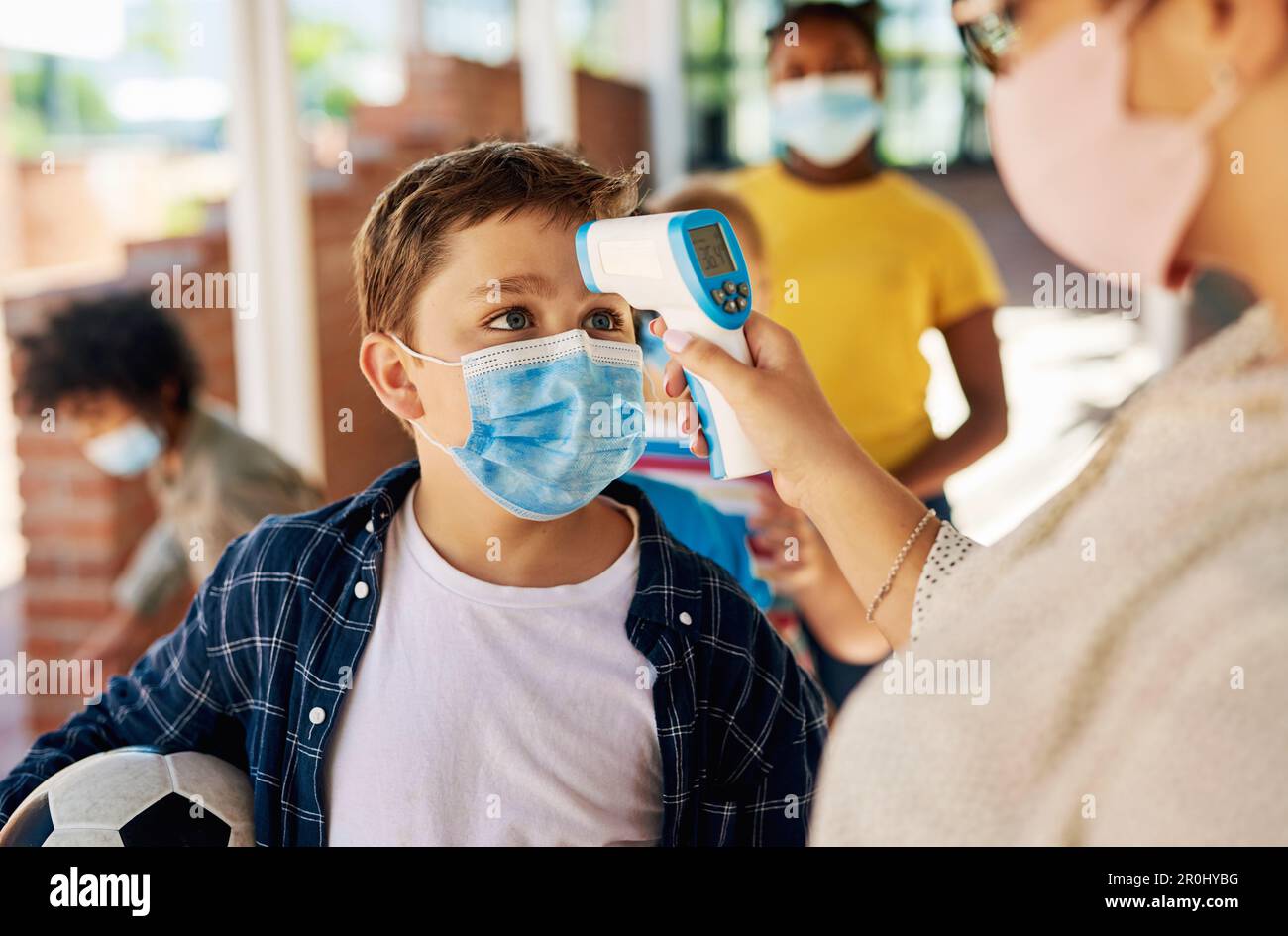 Temperature check please. a young boy wearing a mask and getting his ...