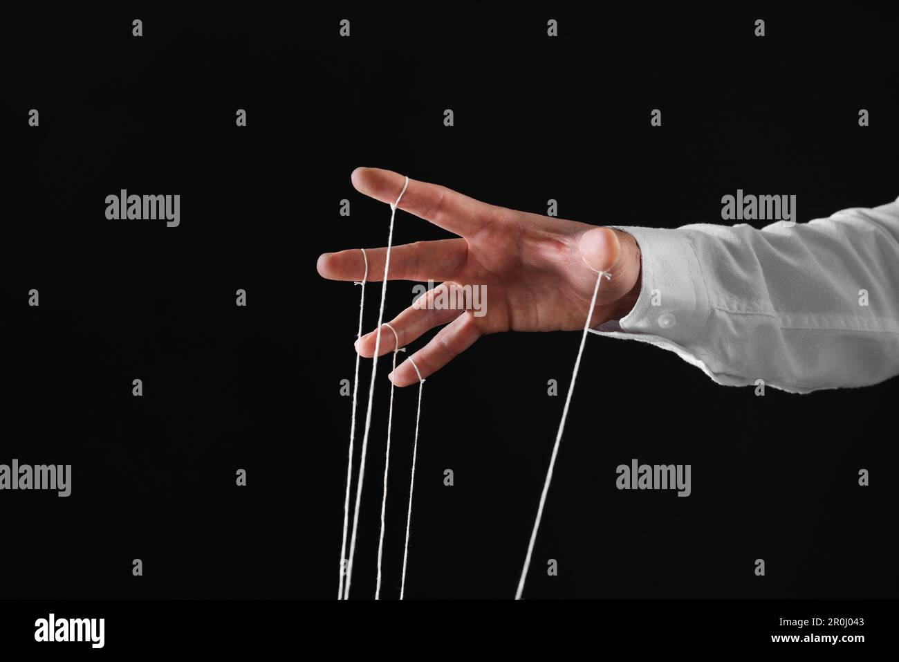 Man pulling strings of puppet on black background, closeup. Space for ...