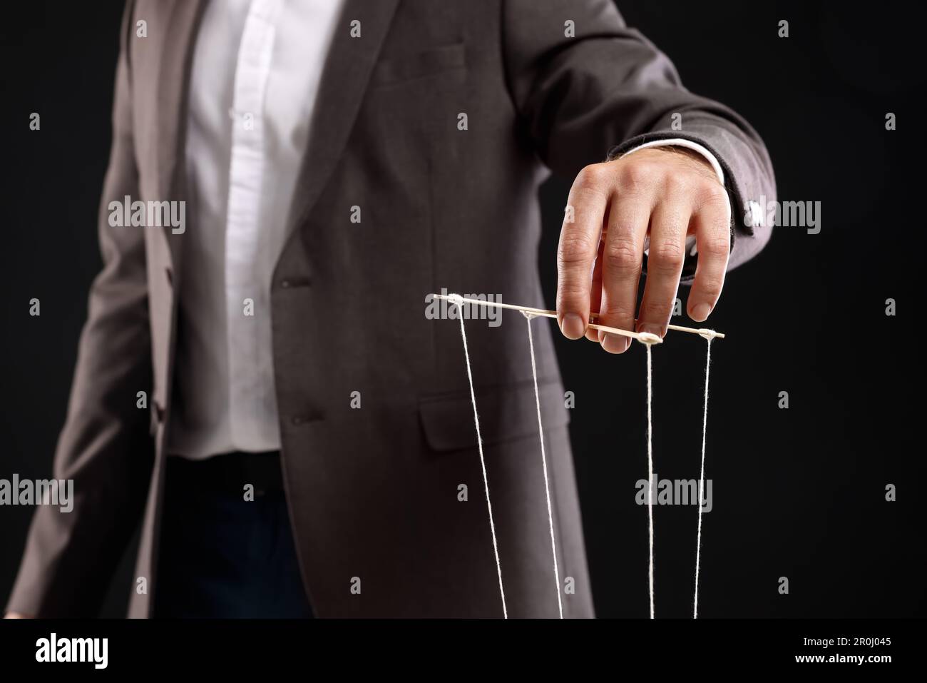 Man in suit pulling strings of puppet on black background, closeup ...