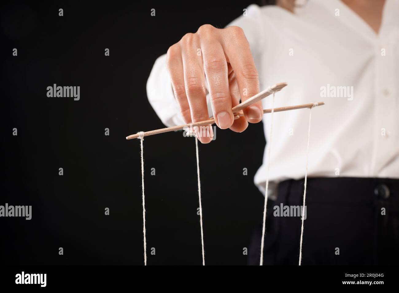 Woman in formal outfit pulling strings of puppet on black background ...