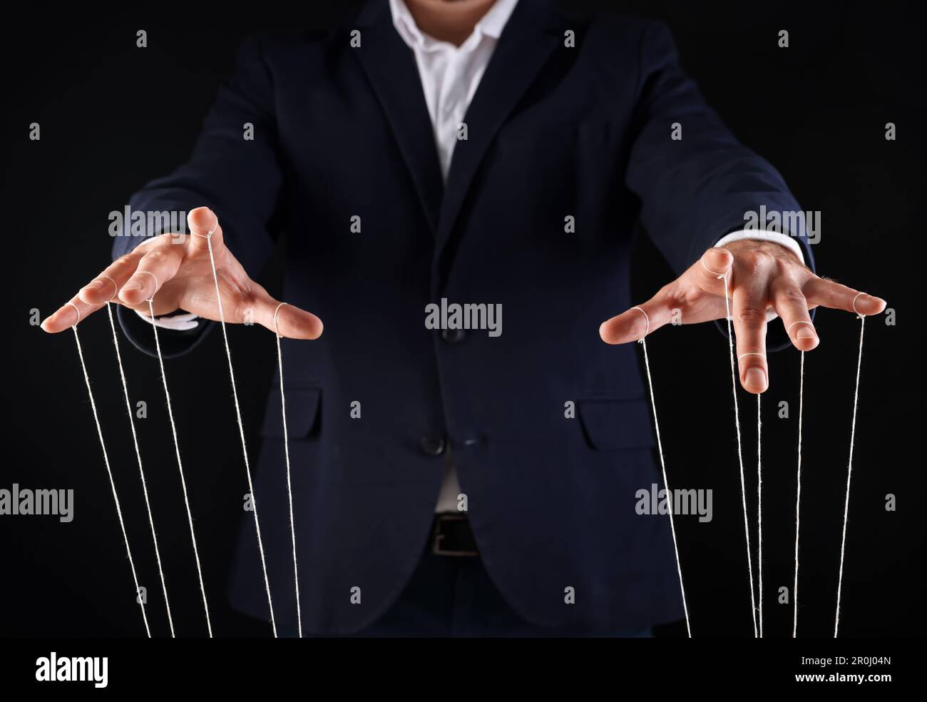 Man in suit pulling strings of puppet on black background, closeup ...