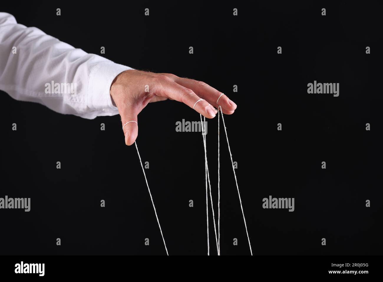 Man pulling strings of puppet on black background, closeup. Space for ...