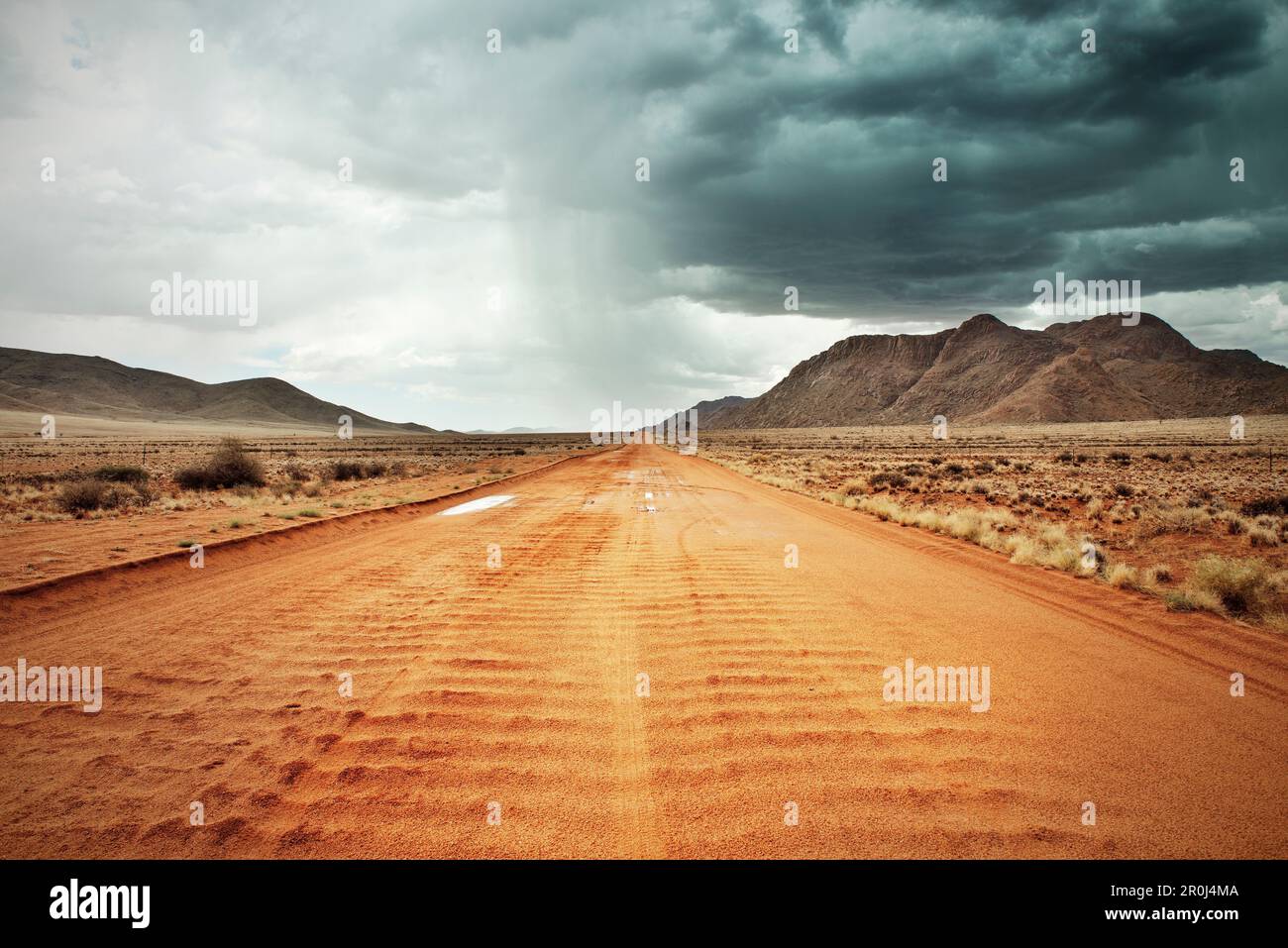 Red sandy road with heavy rainfall and thunderstorm in the distance ...