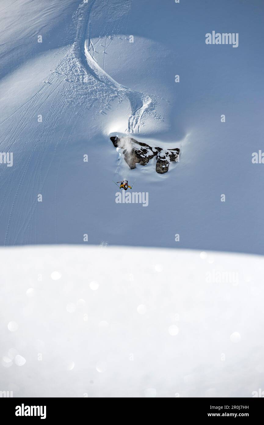 Skier doing a back flip over a small cliff onto a wide-open slope ...
