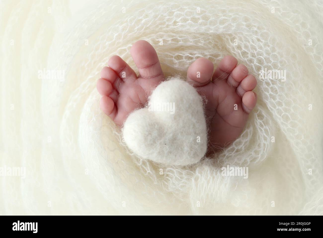 Knitted white heart in the legs of a baby. The tiny foot of a newborn ...