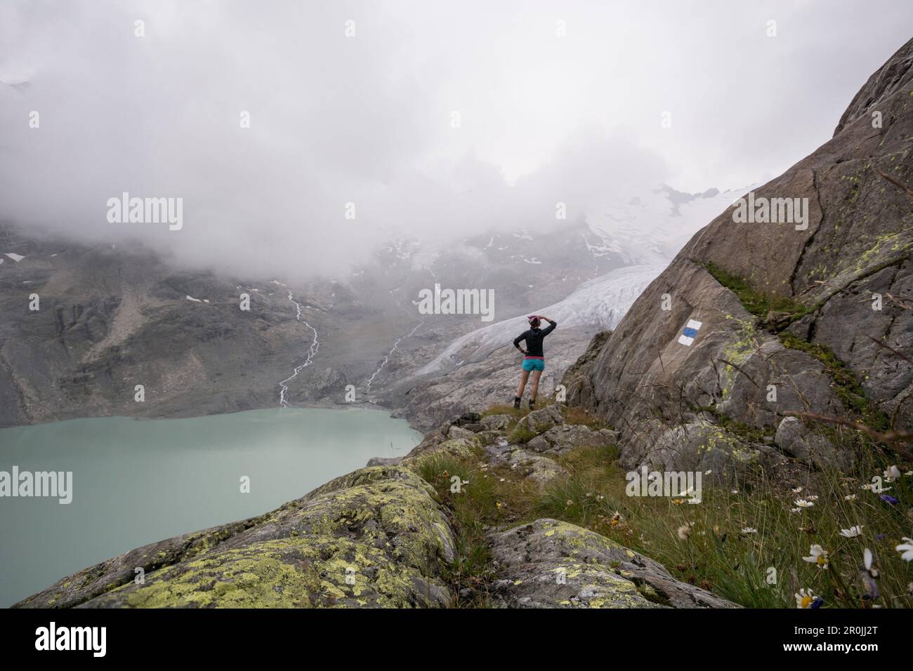 A young female hiker standing on an alpine hiking path with a nice view ...