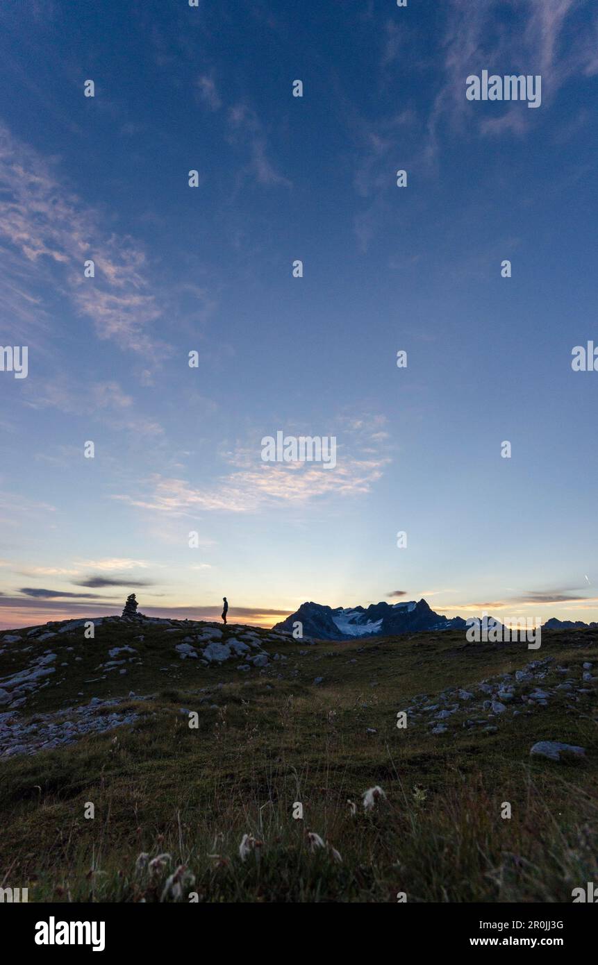 In the first light of the day a hiker is approaching a cairn on the ...