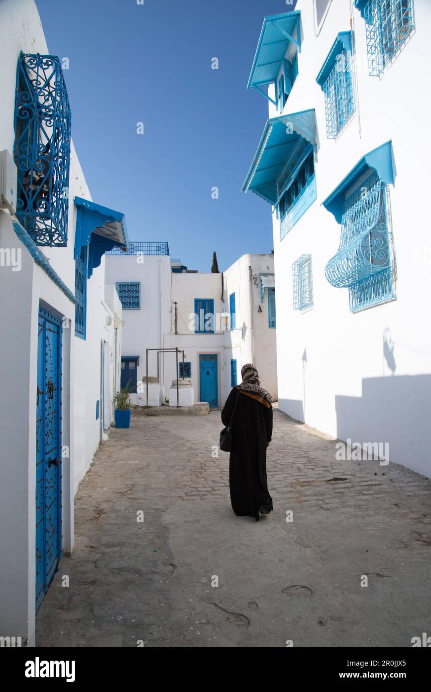 Woman walks along path of buildings with blue windows and white walls ...