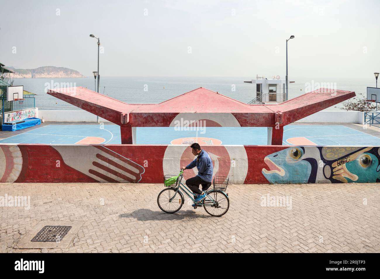 Chinese man on bike passes playing court in front of sea, Cheng Chau ...