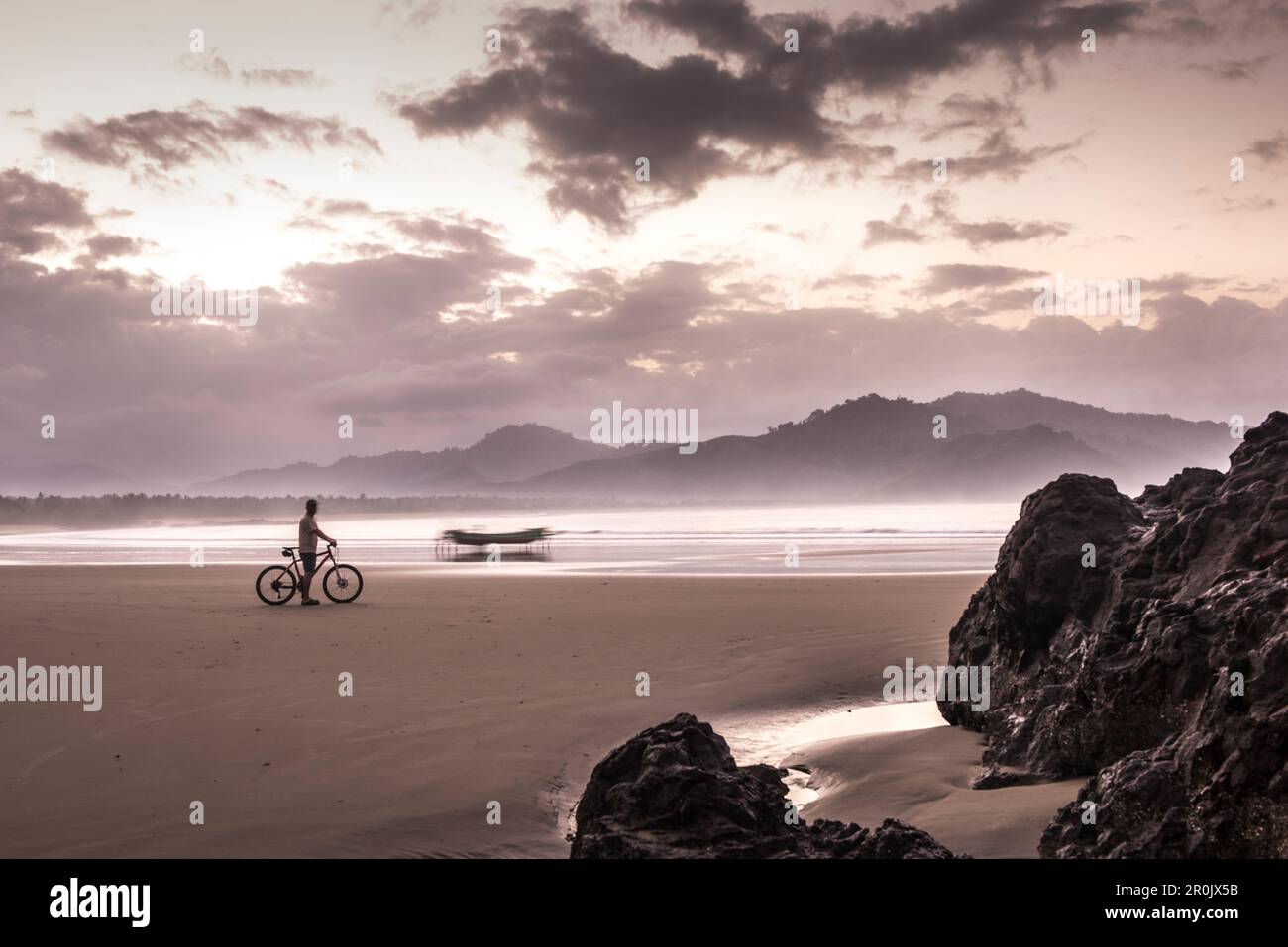 Deserted beach in a bay with cyclist and fishing boat after sunrise ...