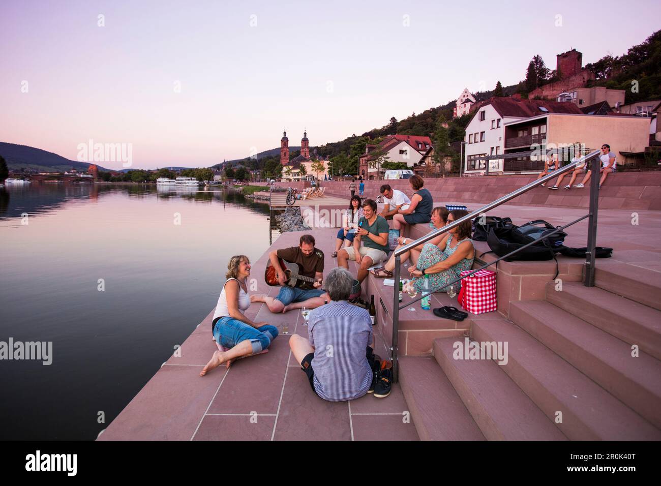 People sing, drink and relax on steps along riverfront of Main river at ...