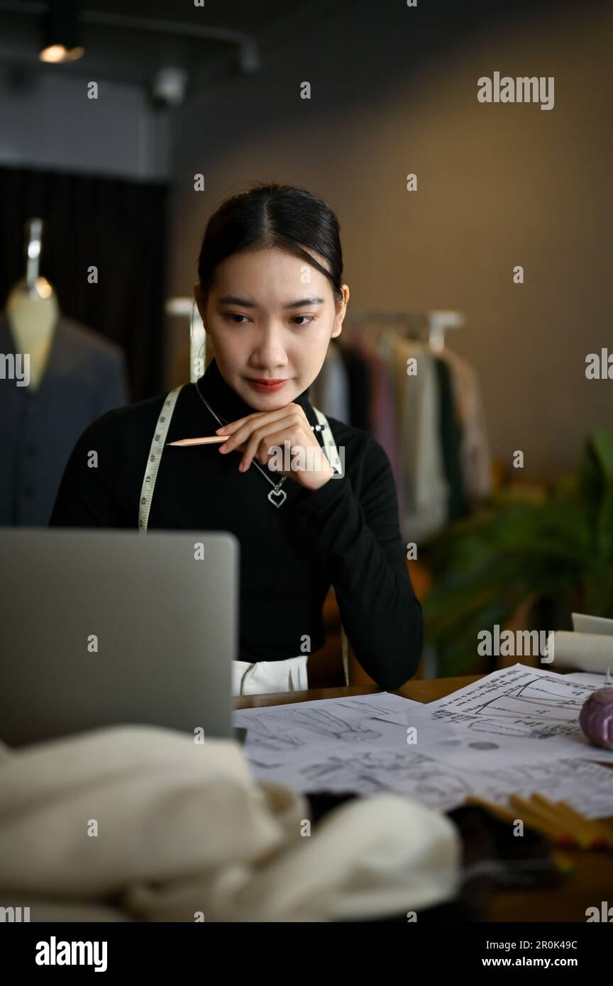 Portrait of an attractive millennial Asian female fashion designer using laptop, planning and ...