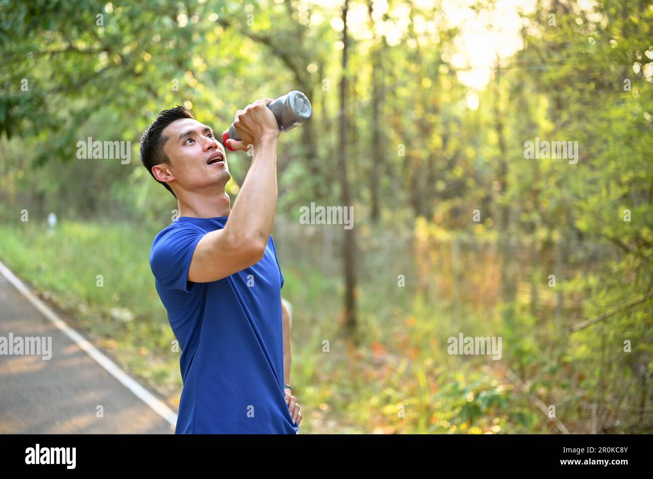 Thirsty and tired millennial Asian male runner in sportswear drinks ...