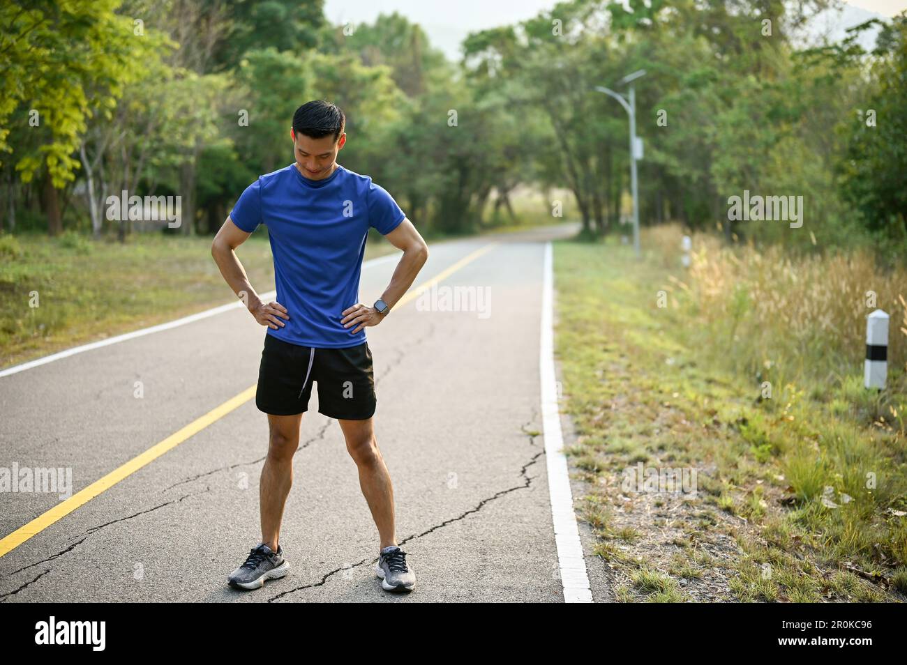 Tired millennial Asian male runner in sportswear rests on the street in ...