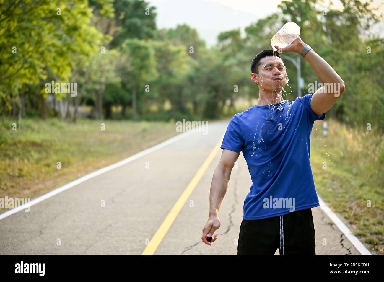 Tired and exhausted millennial Asian male runner pouring water from a ...