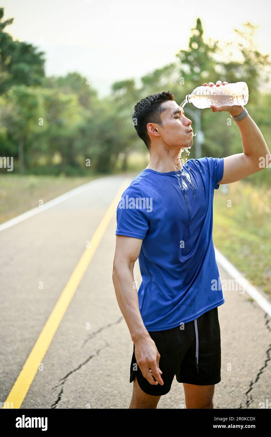 Portrait of thirsty and exhausted Asian man in sportswear pouring water ...