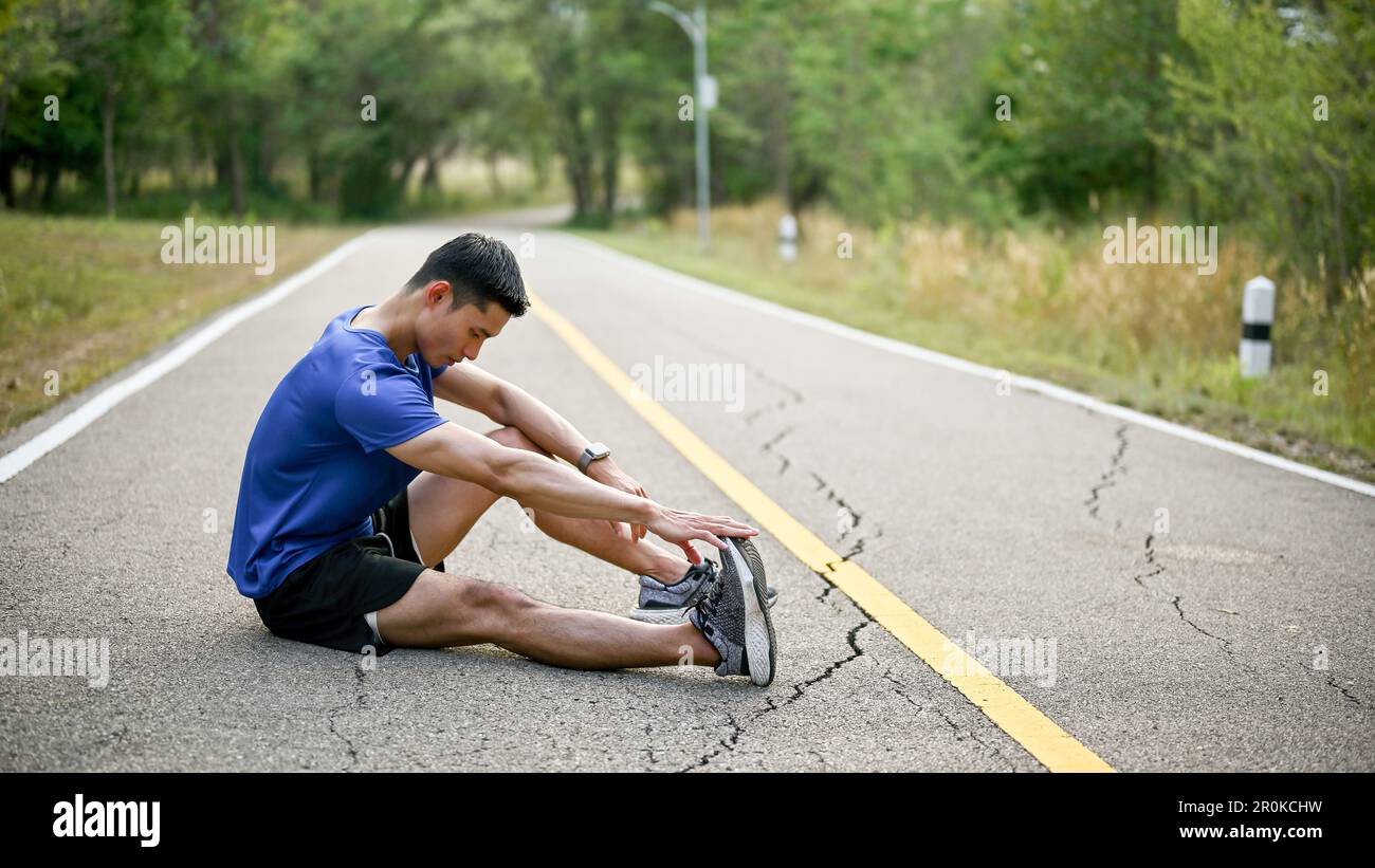 Athletic Asian man having muscle cramped during running, stretching his ...