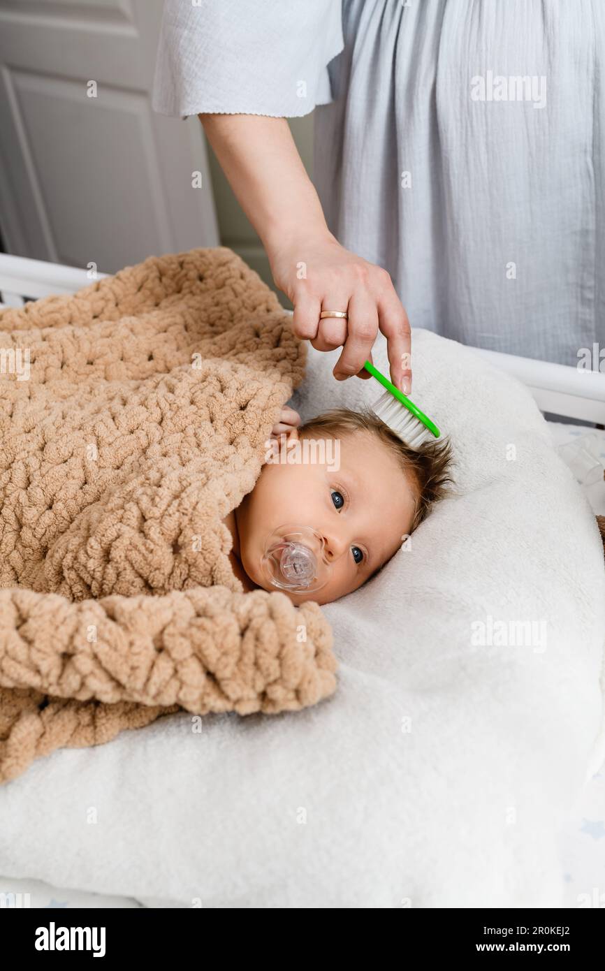 Mother hand brush newborn baby first hair, infant lay in crib covered ...