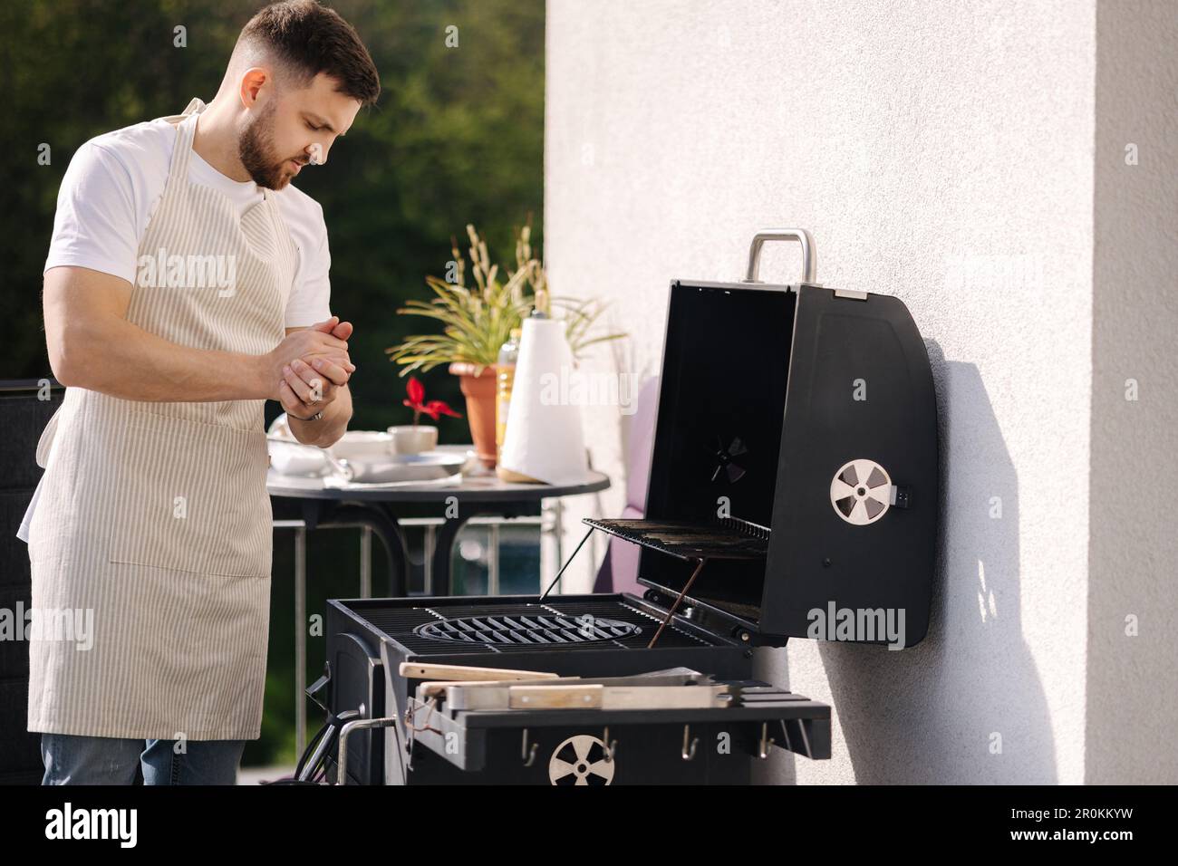 Side view of handsome man try how hot is BBQ grill. Man in apron make ...