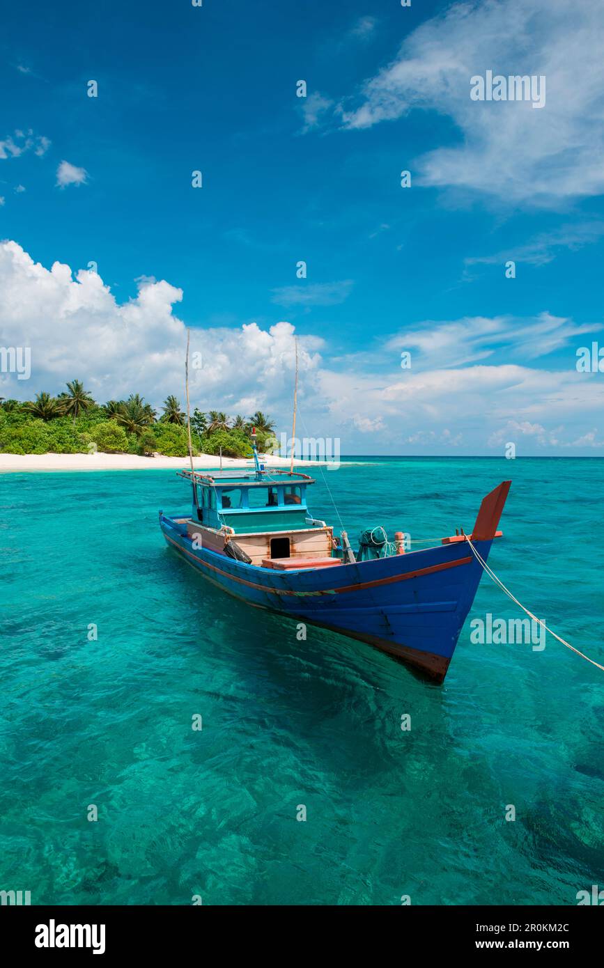 A colorful boat drifts in clear turquoise water off an island, Senua ...