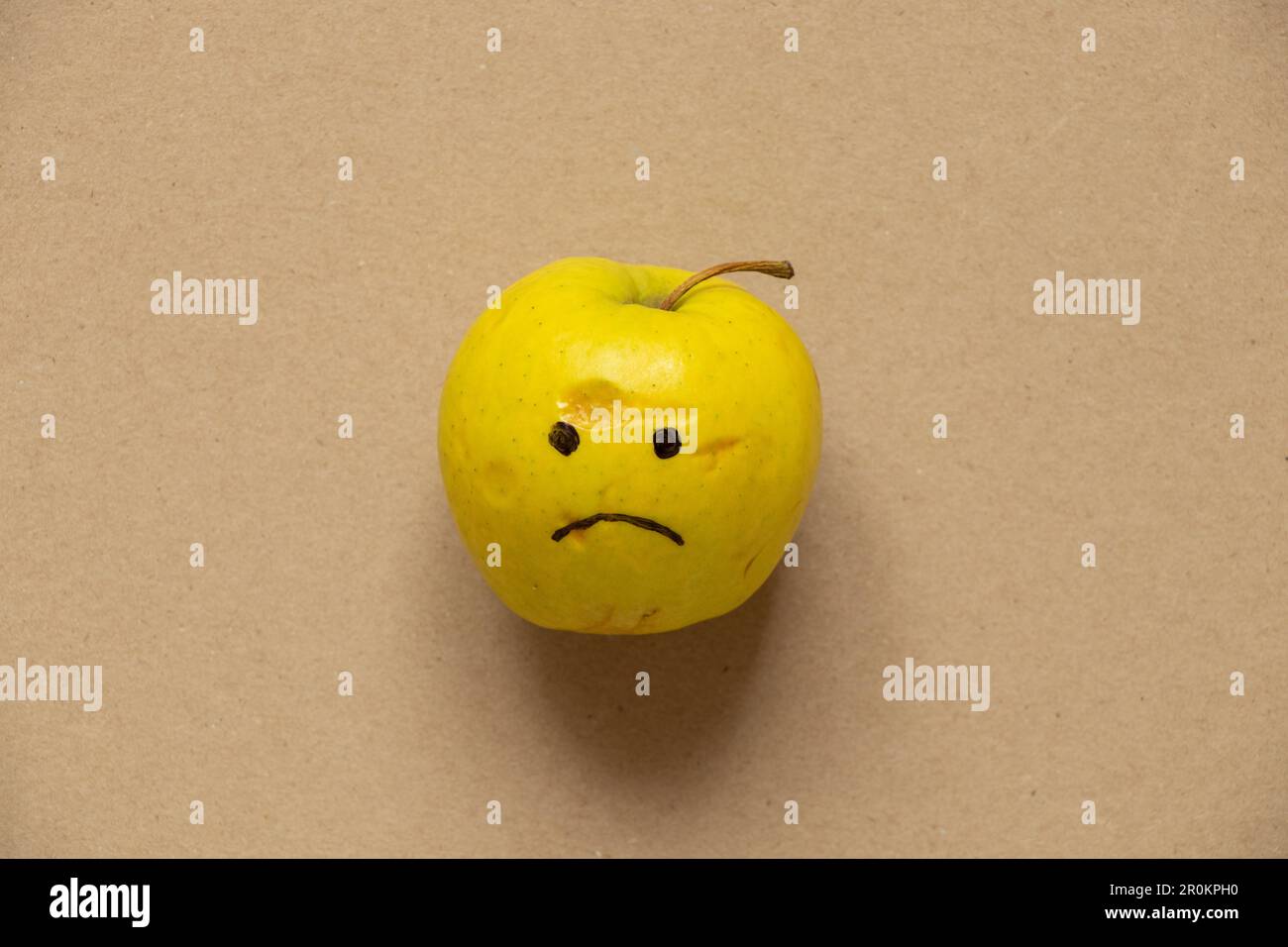 Green missing apple with a sad smile painted on brown paper, sadness ...