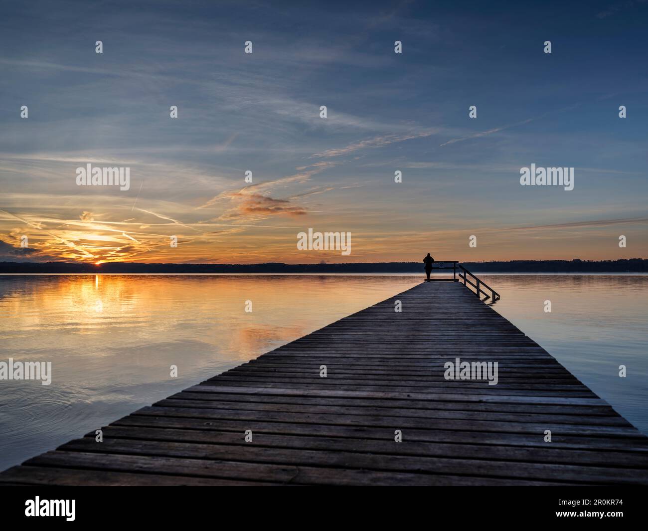 A woman standing on a jetty at sunset on the eastern shore of lake ...