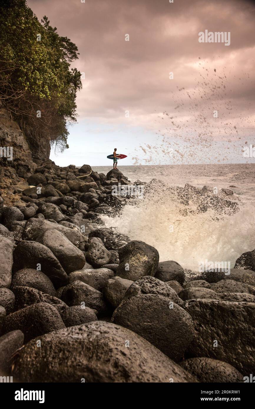 USA, Hawaii, The Big Island, surfer watches the waves on a rocky ...