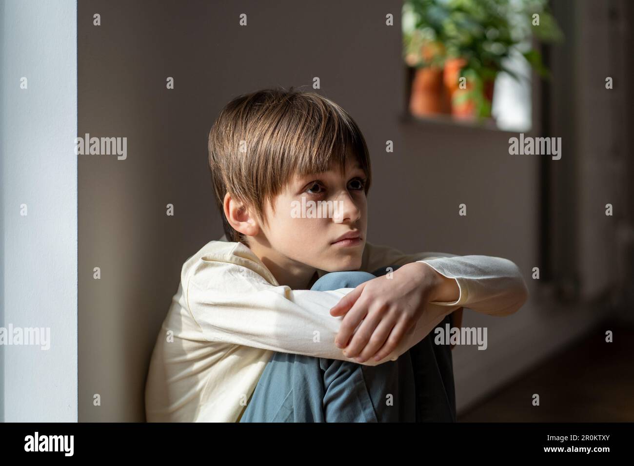 Sad worried teen boy sitting on floor embracing knees at home near ...
