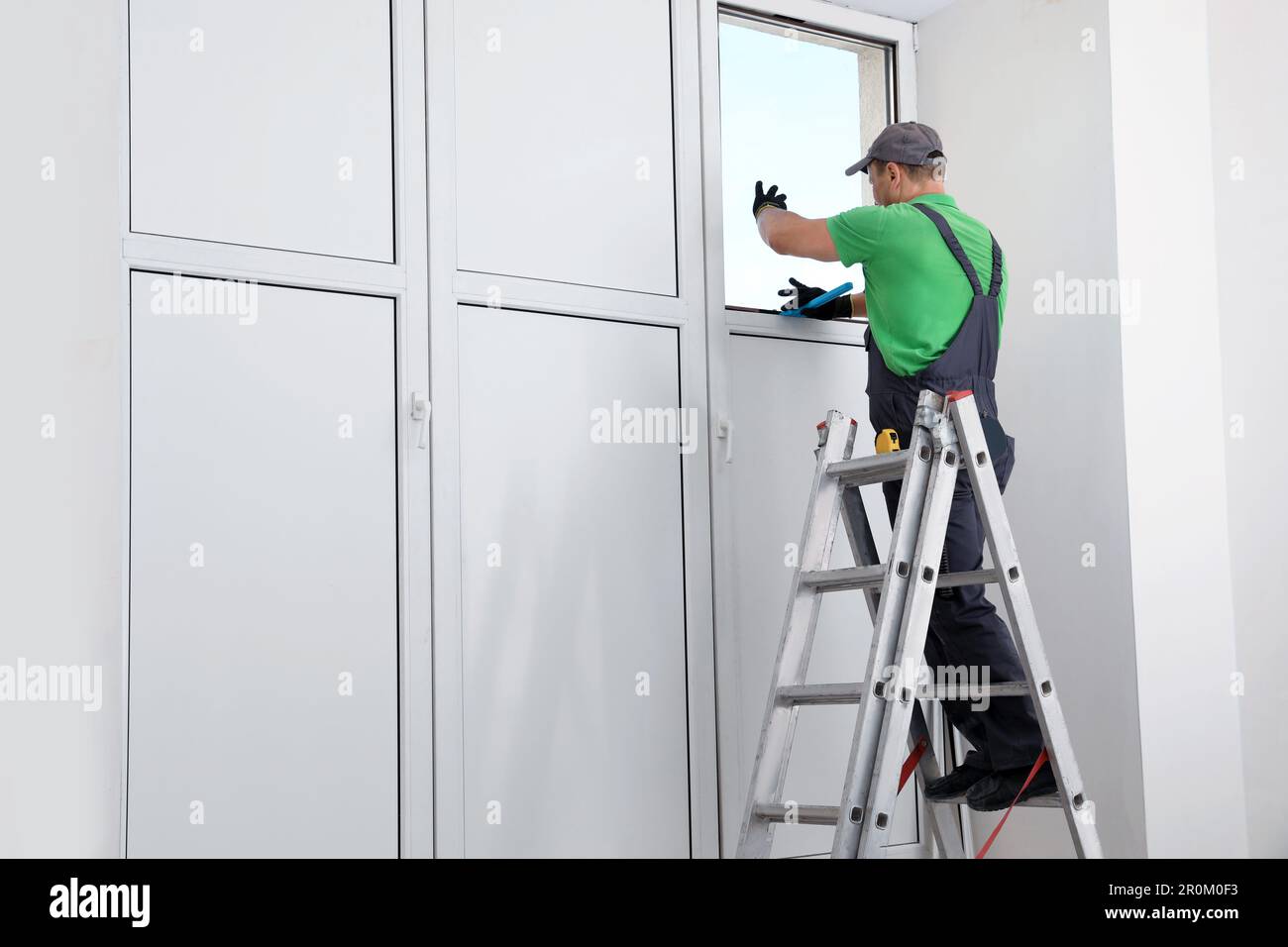 Worker on folding ladder installing window indoors Stock Photo - Alamy
