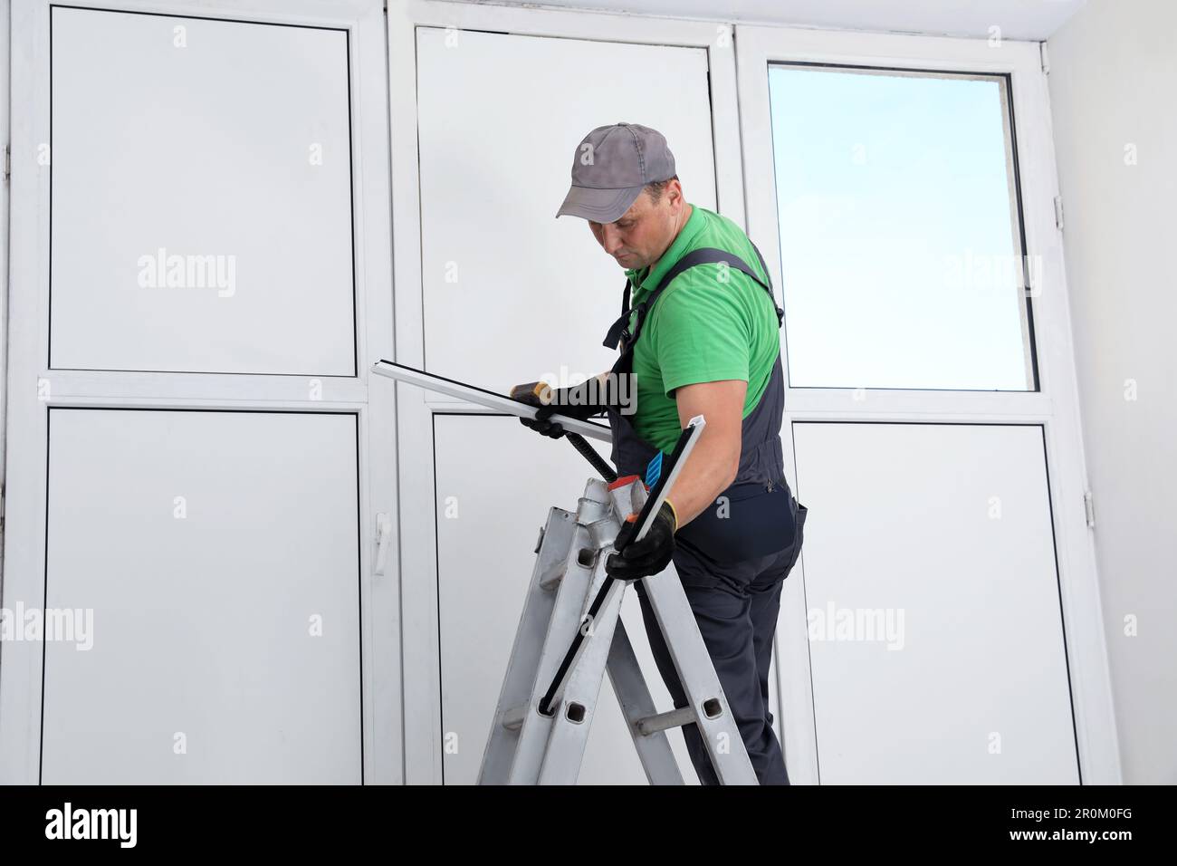 Worker on folding ladder installing window indoors Stock Photo - Alamy