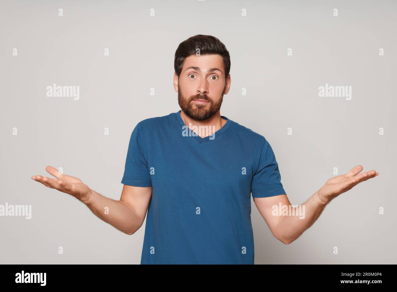 Handsome bearded man shrugging shoulders on light grey background Stock ...