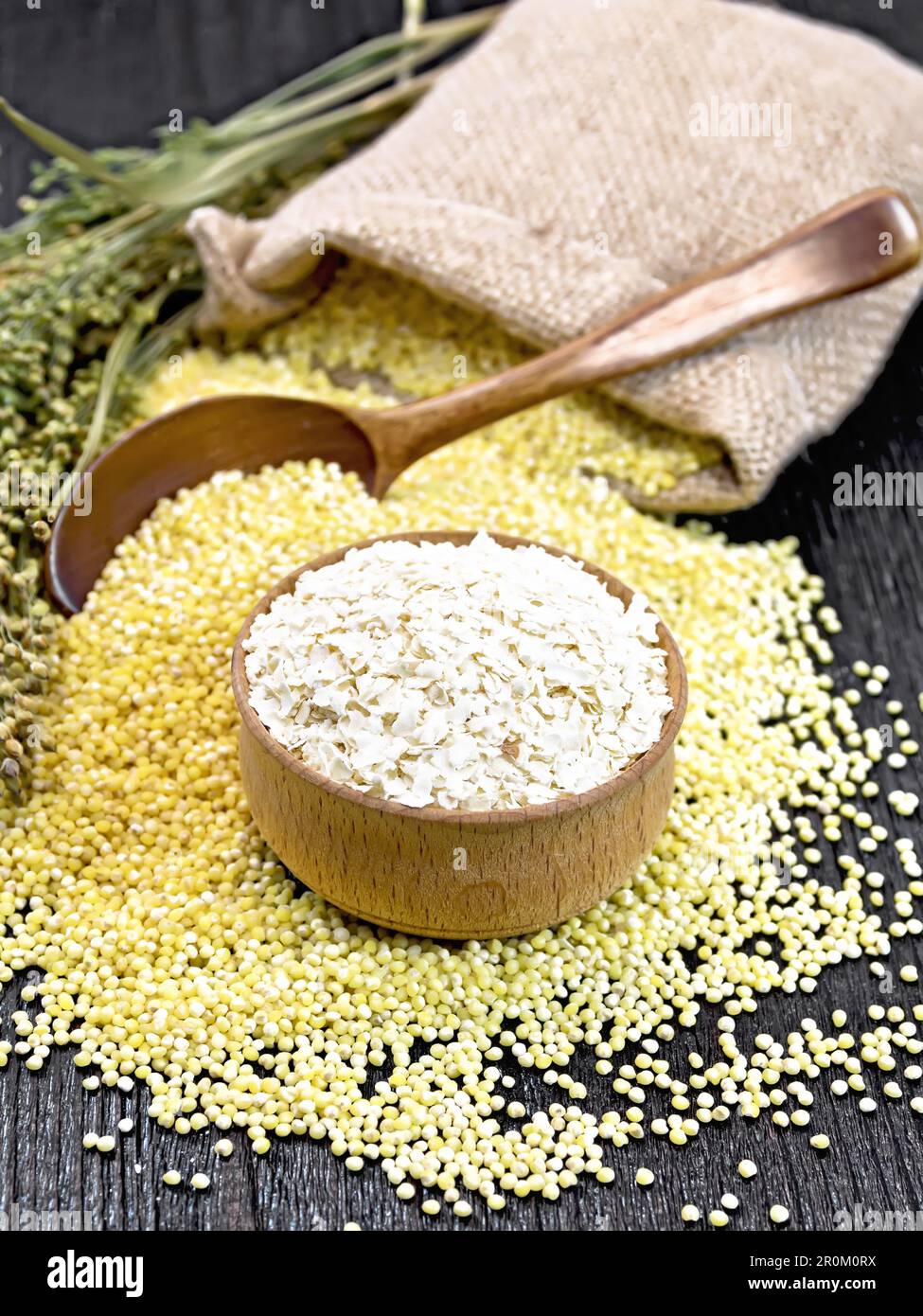 Millet flakes in a bowl, groats on the table, in a spoon and a bag of ...
