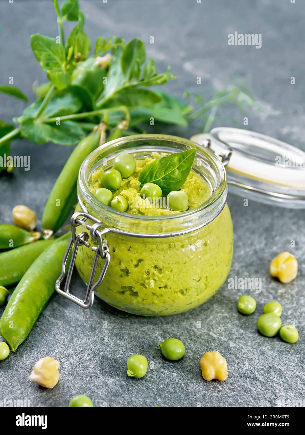 Hummus from green peas and chickpeas in a glass jar, pea pods on ...
