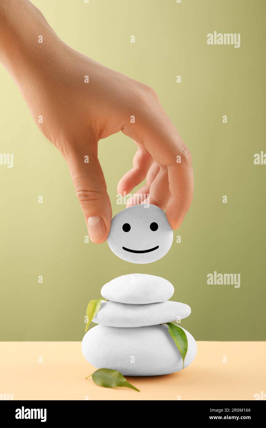 Woman putting stone with drawn happy face on stack, closeup Zen concept ...