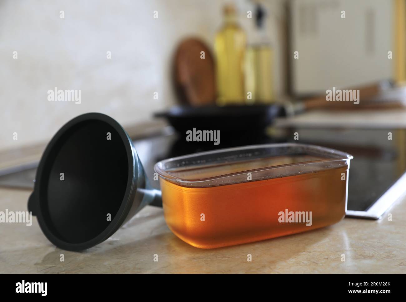 Container with used cooking oil and funnel near stove on kitchen ...