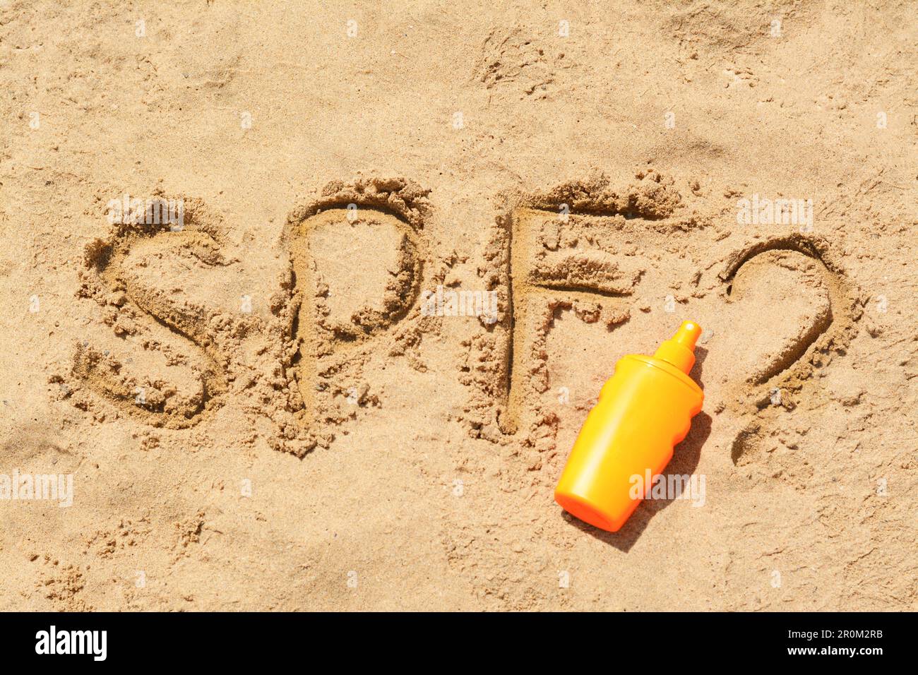 Abbreviation SPF and question mark written on sand, blank bottle of ...