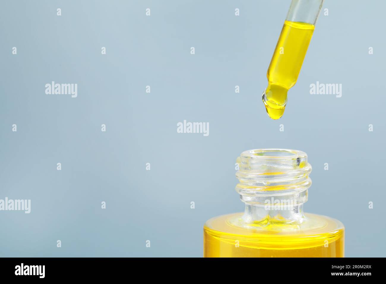 Dripping yellow serum from pipette into bottle on grey background ...