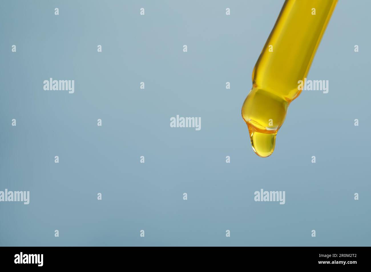 Dripping yellow serum from pipette on grey background, closeup. Space ...