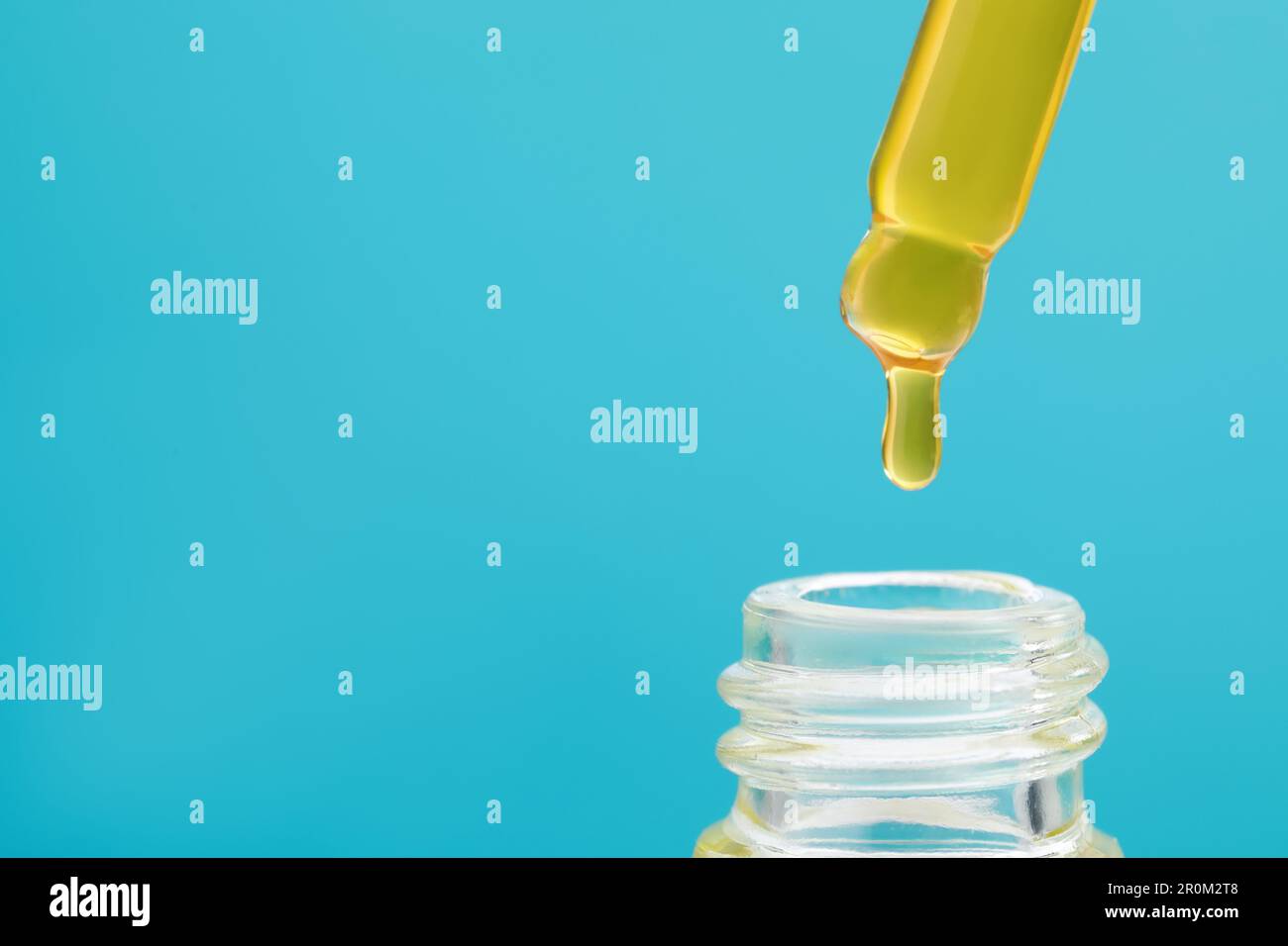 Dripping yellow serum from pipette into bottle on light blue background ...