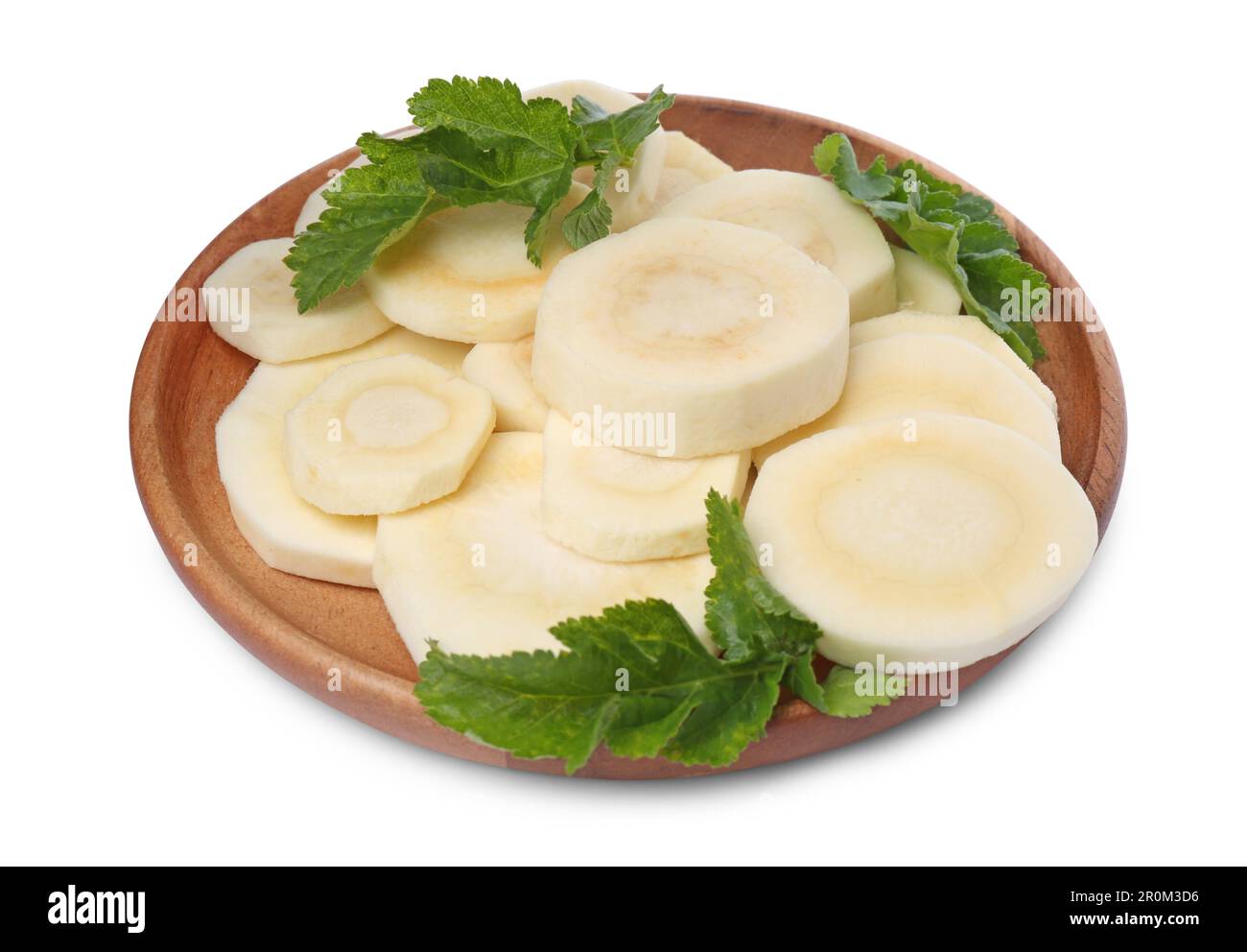 Cut fresh ripe parsnip with leaves in wooden plate on white background ...