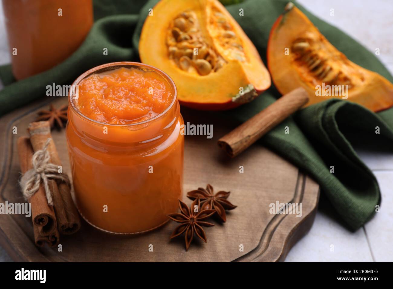 Jar of delicious pumpkin jam and ingredients on tiled surface, closeup ...