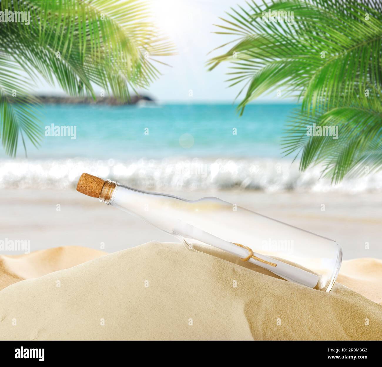 Corked glass bottle with rolled paper note on sandy beach with palms ...