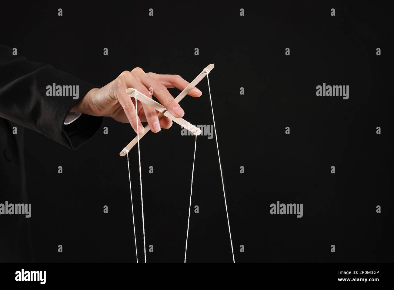 Woman pulling strings of puppet on black background, closeup. Space for ...