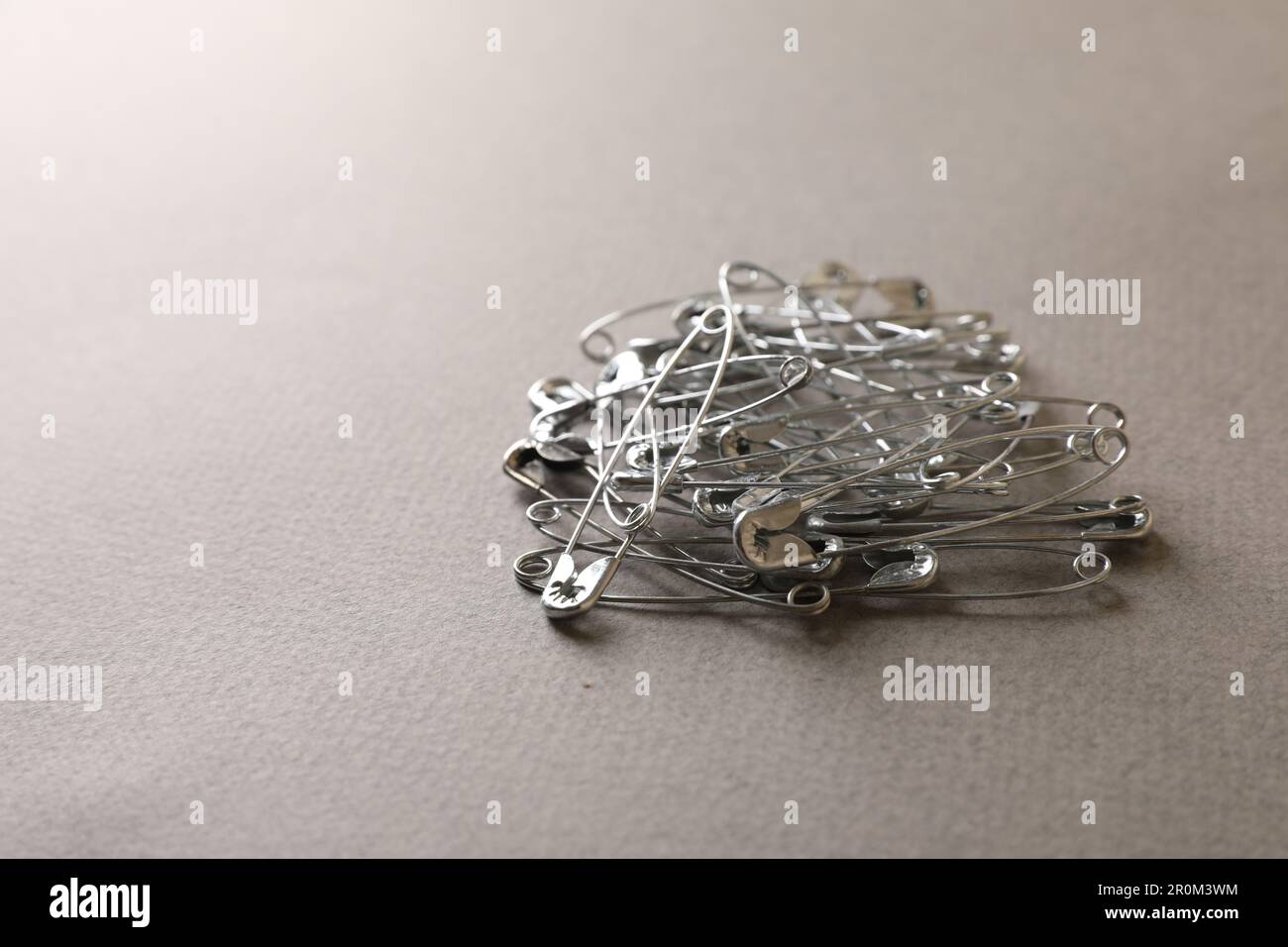 Pile of safety pins on light grey textured background, space for text ...