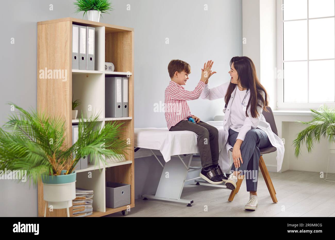 Smiling female doctor giving high five to patient boy in medical office ...