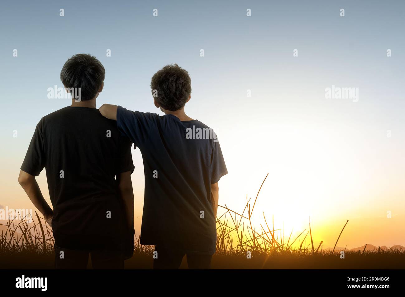 Rear view of two men standing with sunset scene background ...