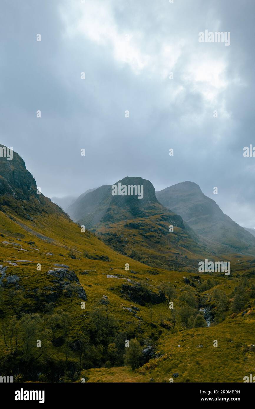 A picturesque mountain landscape featuring a rolling grassy hill dotted ...