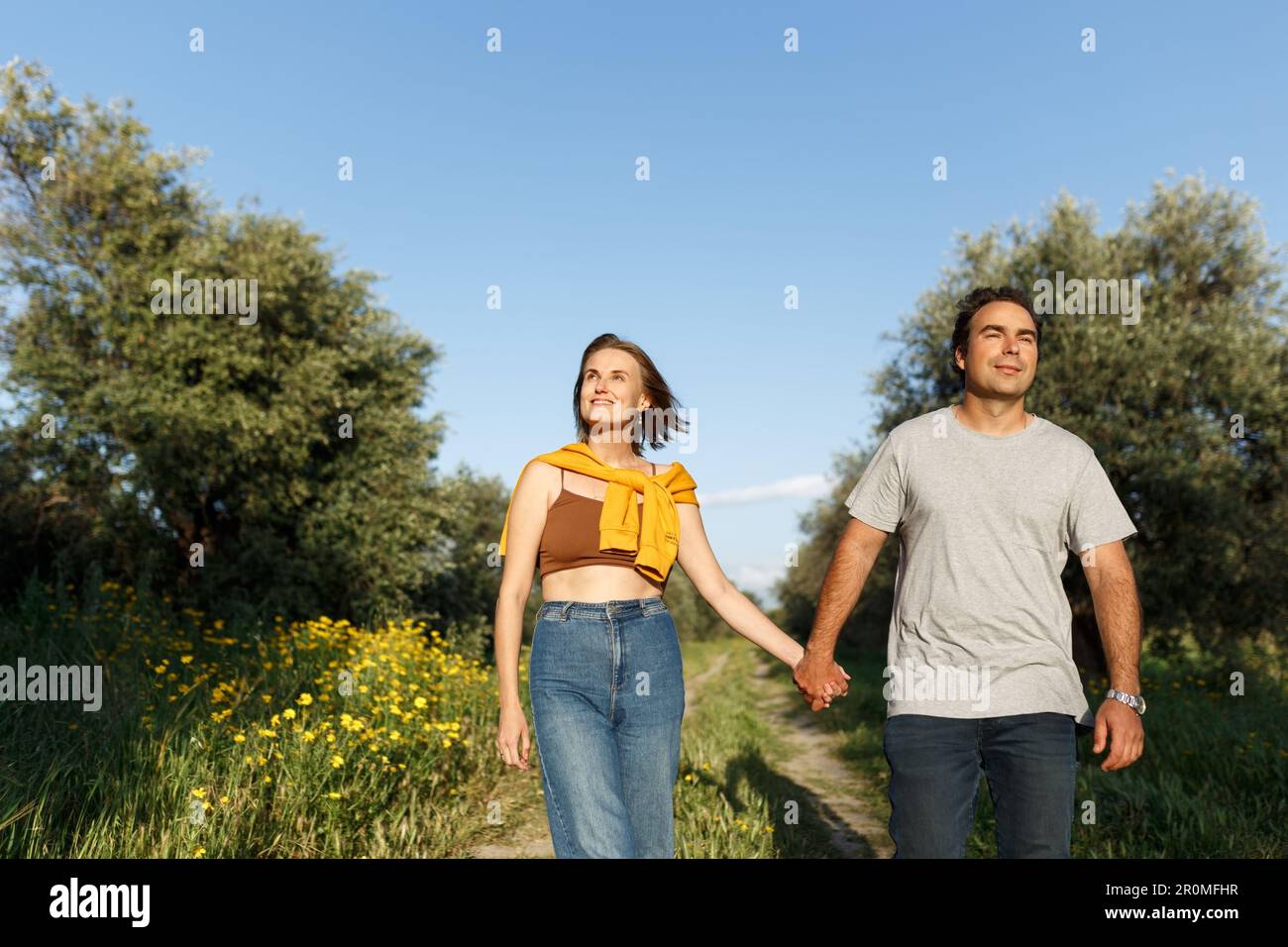 Outdoor shot of young couple in love walking on pathway through grass ...